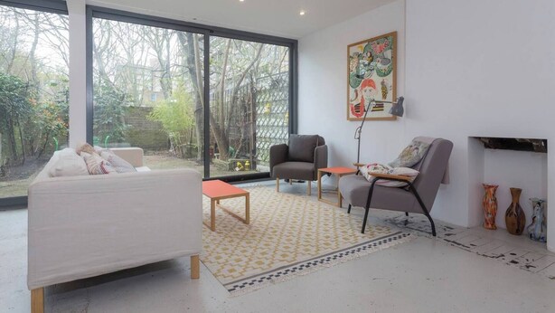 Uma sala de estar moderna com uma janela ampla, um sofá, uma poltrona, uma mesinha e um quadro na parede.