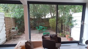 Uma sala de estar moderna com uma grande porta de vidro deslizante que dá para um jardim com cadeiras verdes e plantas em vasos.