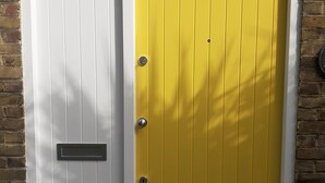 Uma porta amarela com moldura branca, uma abertura para correspondência e uma fechadura.