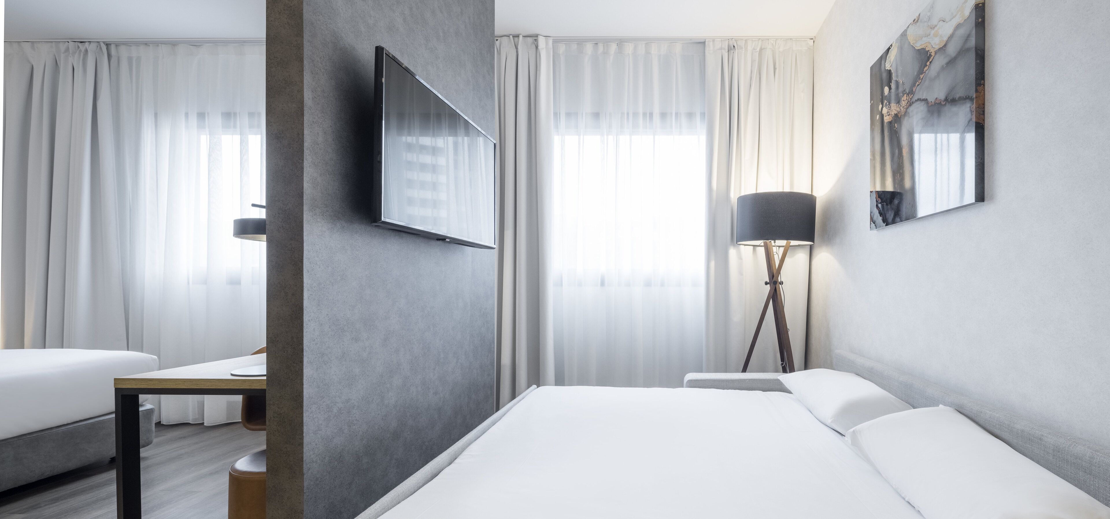 Quarto de hotel moderno com uma cama grande, uma escrivaninha, uma televisão de tela plana na parede e um abajur.