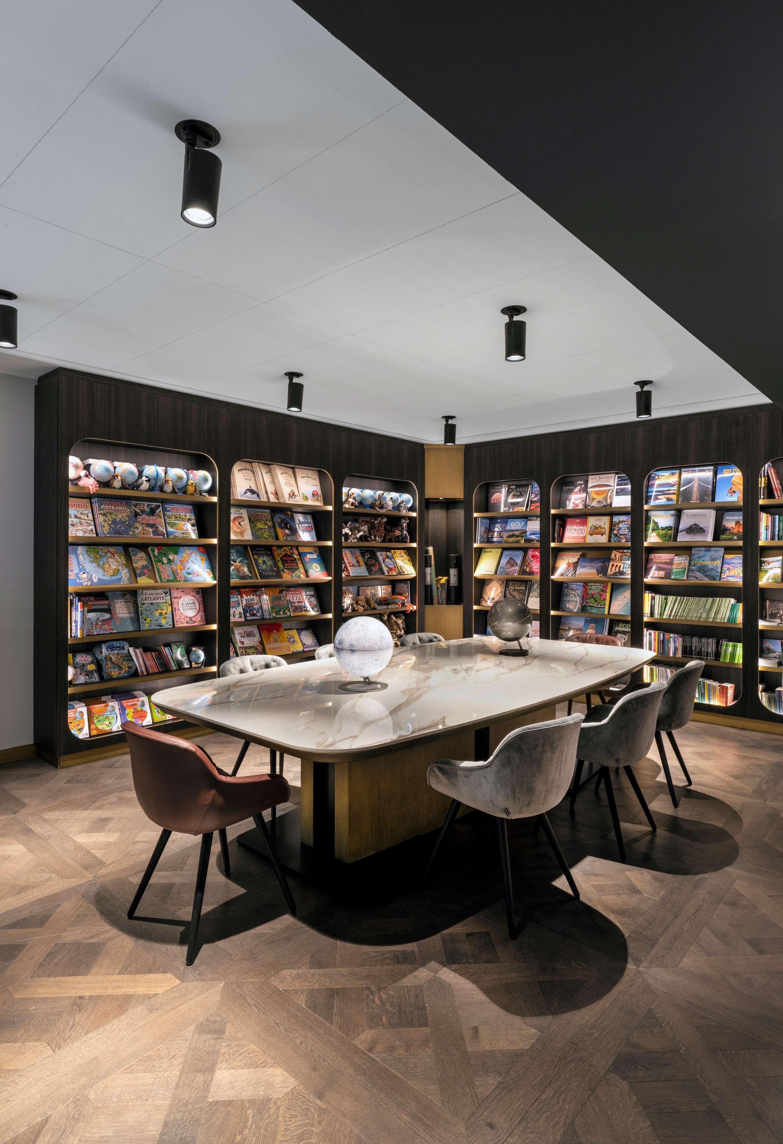 Uma biblioteca moderna com uma grande mesa de mármore, várias estantes e assentos confortáveis.