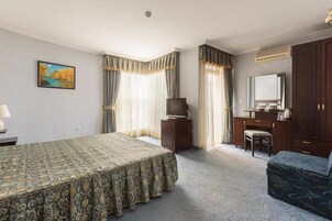 Quarto de hotel com cama, escrivaninha com cadeira, televisão, espelho e cômoda.