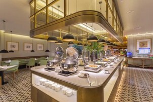Espaço de café da manhã de hotel com buffet, incluindo diversos alimentos e um ponto de café.