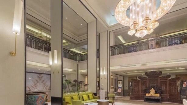 Um hall amplo com um grande candelabro, um sofá verde e uma estátua decorativa.