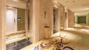 Um corredor com paredes e pisos de mármore, um tapete estampado e uma porta que dá para um quarto.