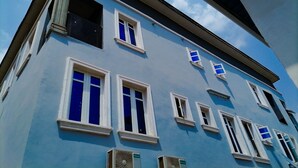 Um edifício com várias andares, fachada azul, molduras de janela brancas e diversas janelas.