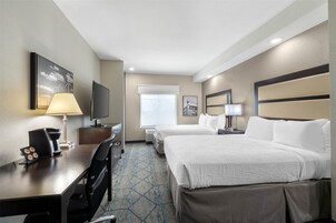 Quarto de hotel com duas camas, uma escrivaninha com cafeteira, televisão e janela com persianas.