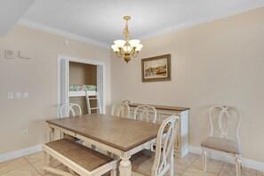 Uma sala de jantar com uma mesa de madeira, cadeiras brancas, um candelabro e um quadro na parede.
