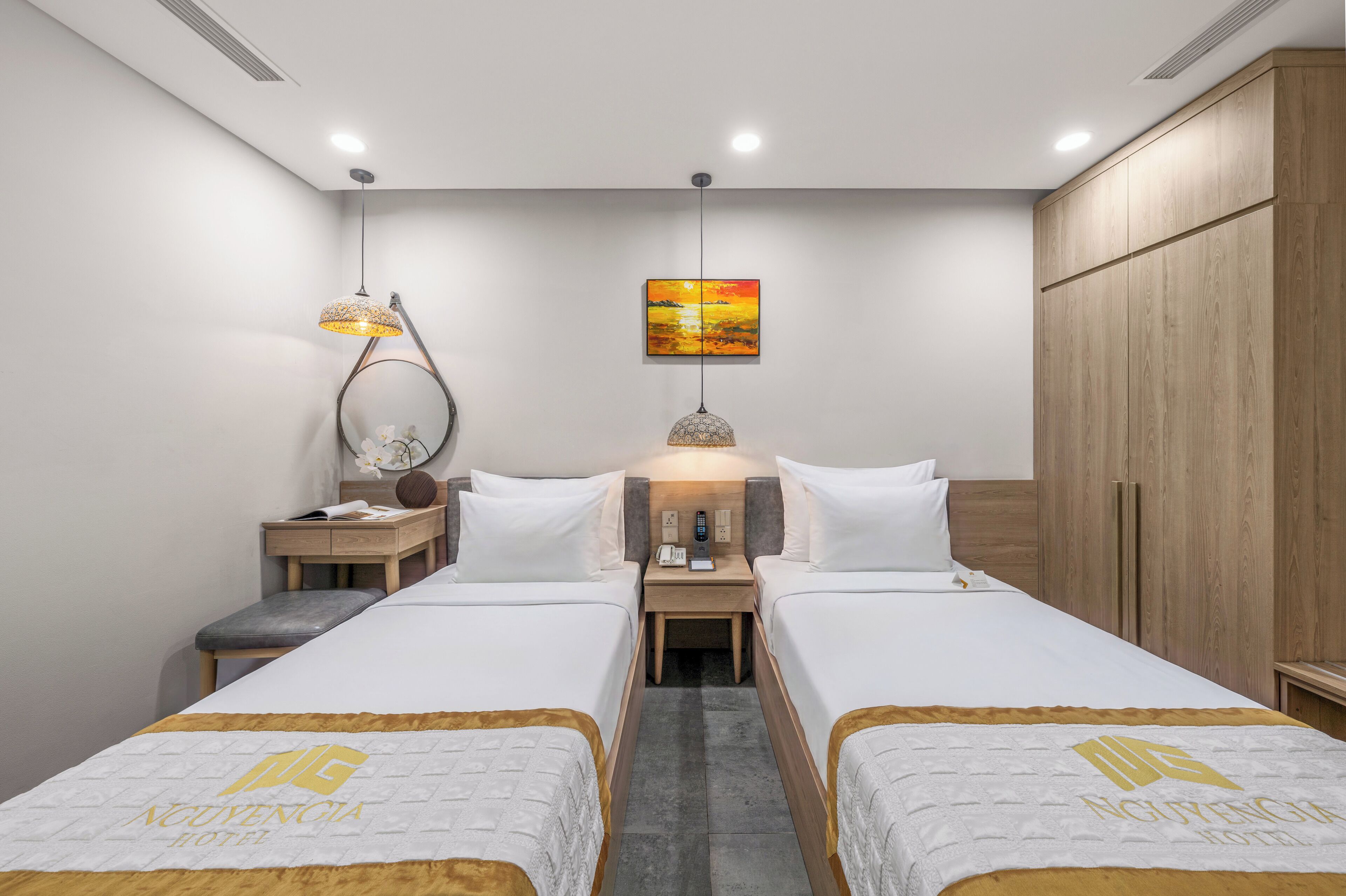 Quarto de hotel com duas camas, uma escrivaninha, um guarda-roupa e um quadro na parede.