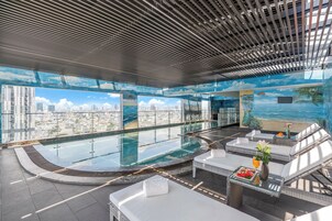 Piscina infinita no terraço com vista para a cidade, área de estar com assentos e um mural de uma paisagem praiana.