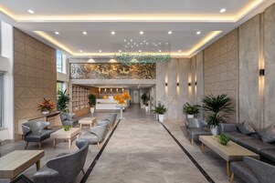 Um saguão de hotel com balcão de recepção, área de estar e uma parede decorativa.