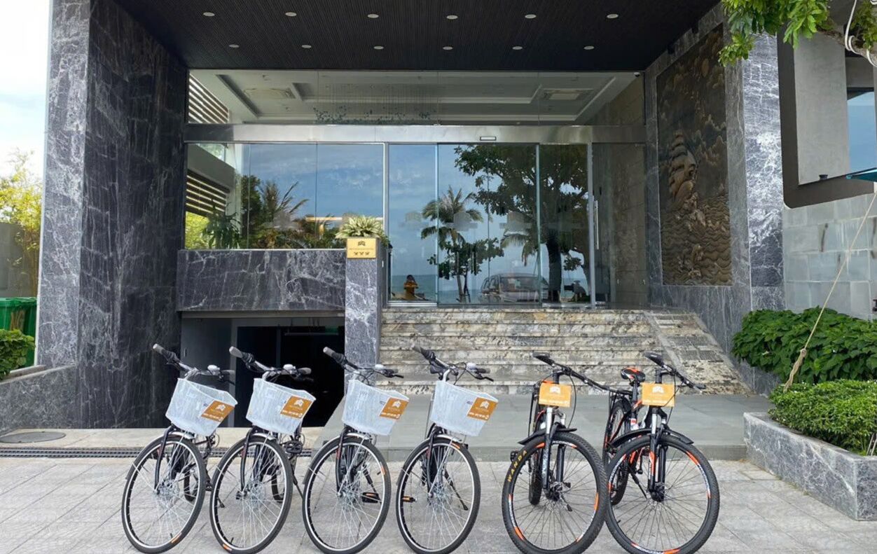 Entrada de um edifício moderno com fachada de vidro, parede de pedra e vários bicicletas com cestas.