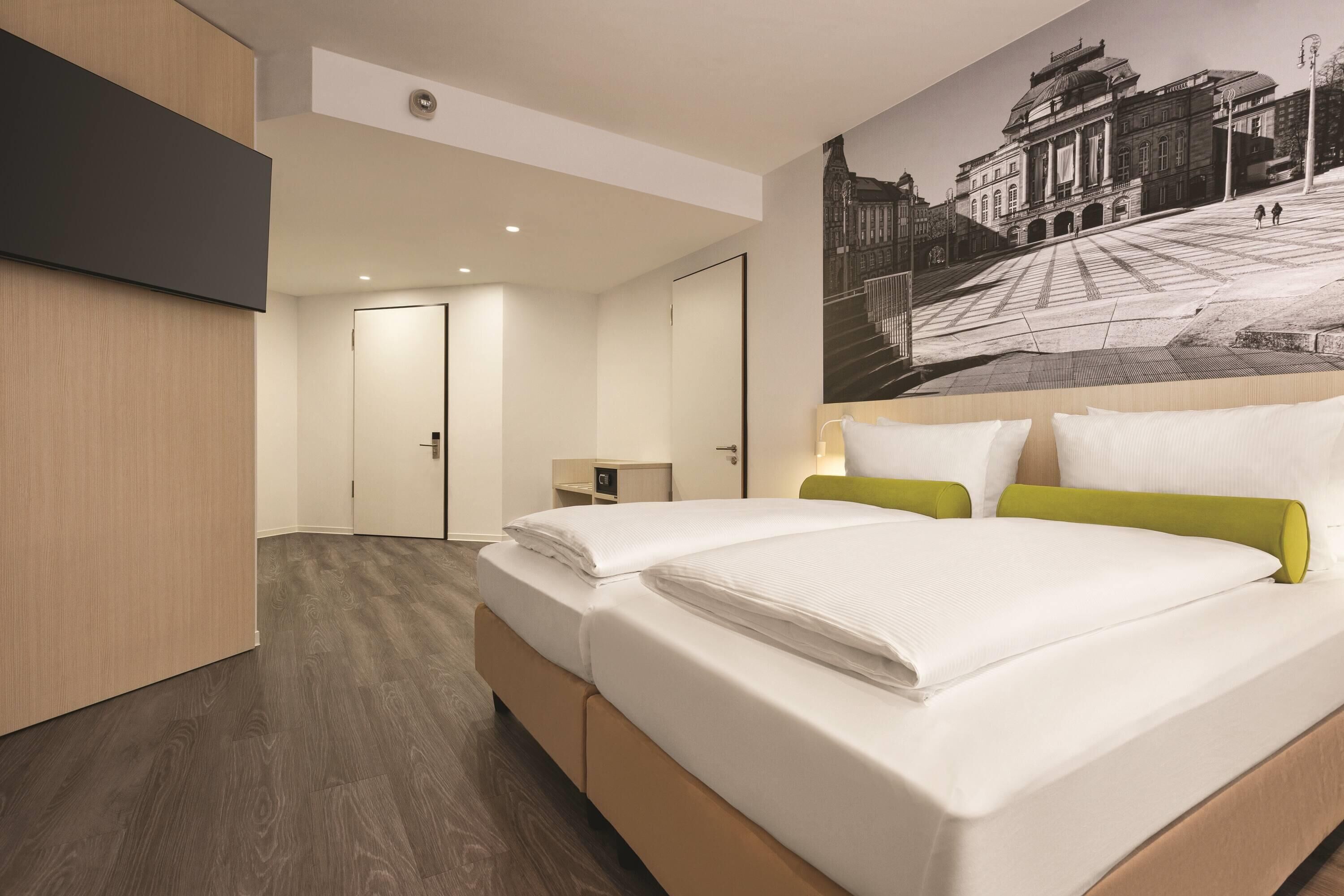 Quarto de hotel com cama grande, escrivaninha, guarda-roupa e televisão na parede.