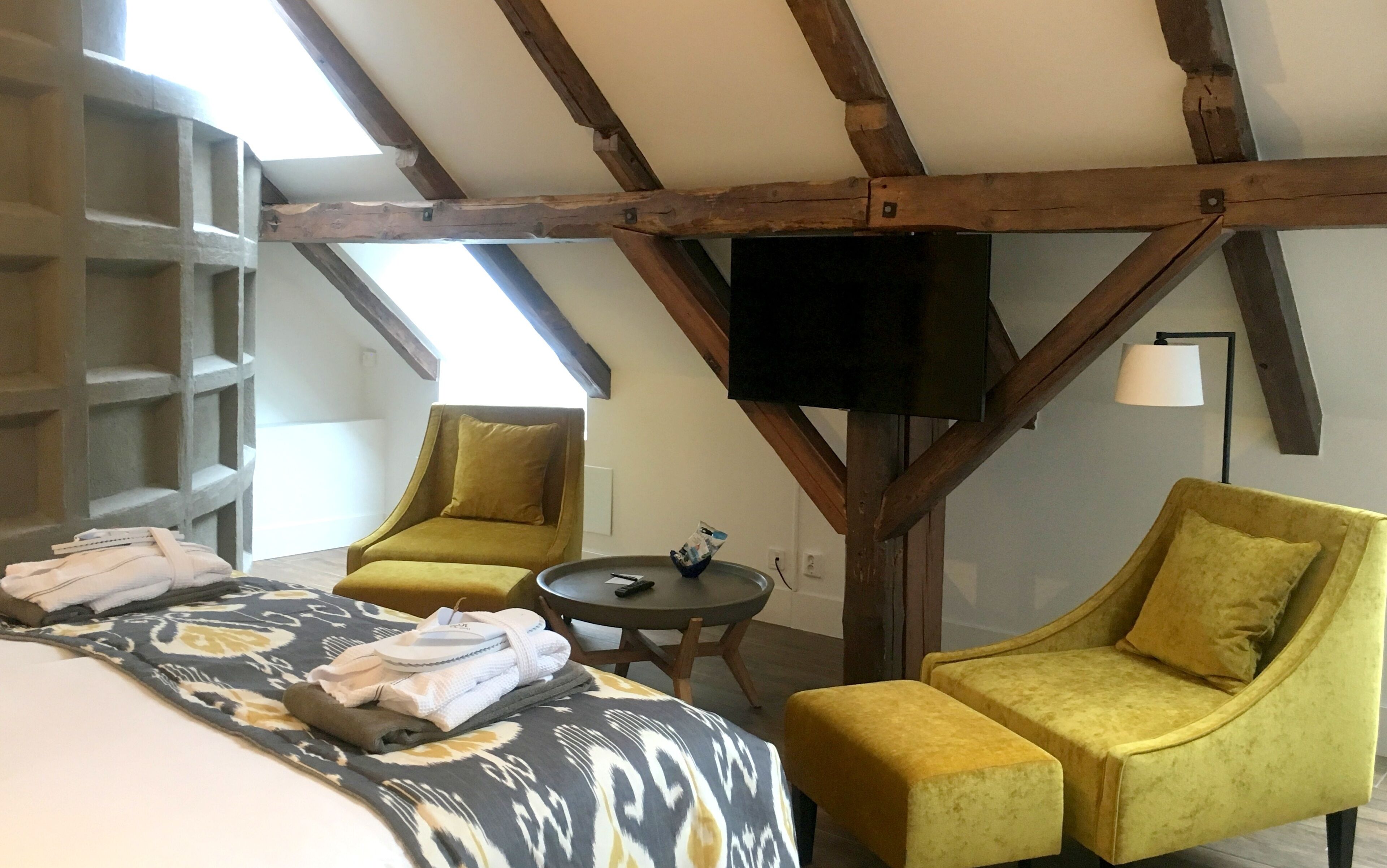 Um quarto com uma cama, duas poltronas, uma mesinha, uma televisão e uma estante de livros.