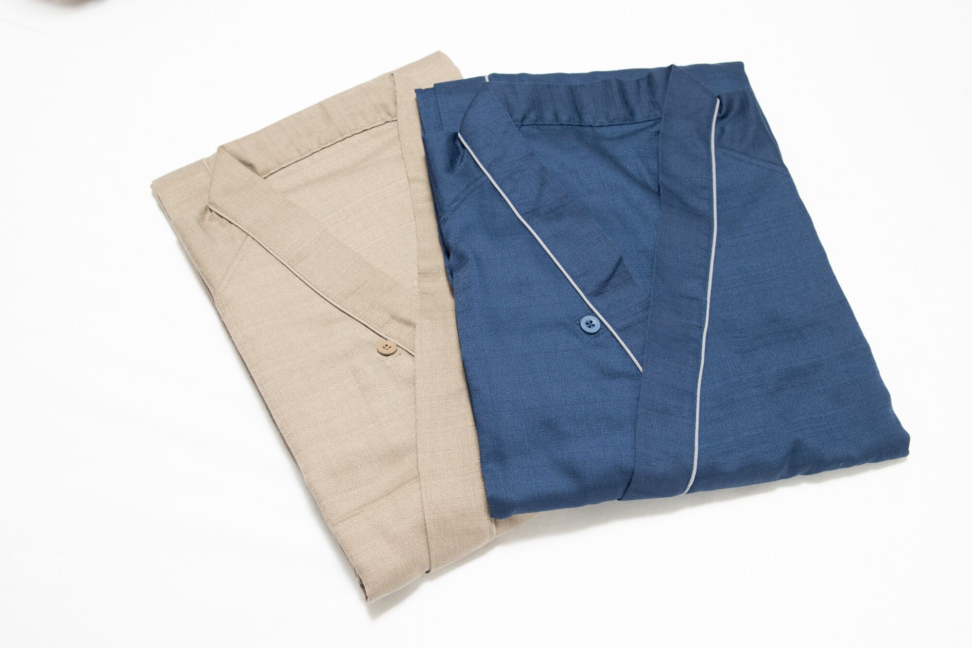 Duas camisas dobradas, uma bege e outra azul, sobre um fundo branco.