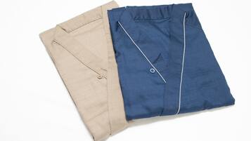 Duas camisas dobradas, uma bege e outra azul, sobre um fundo branco.