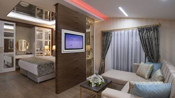 Quarto de hotel moderno com cama, sofá, televisão e escrivaninha.