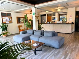 Um lobby moderno com um sofá seccional cinza, uma mesa de centro de madeira e um balcão de recepção.