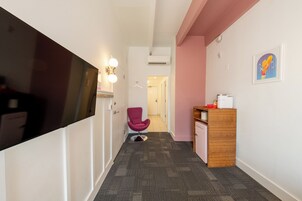 Um corredor com televisão de tela plana, uma cadeira rosa, um armário de madeira e um quadro na parede.