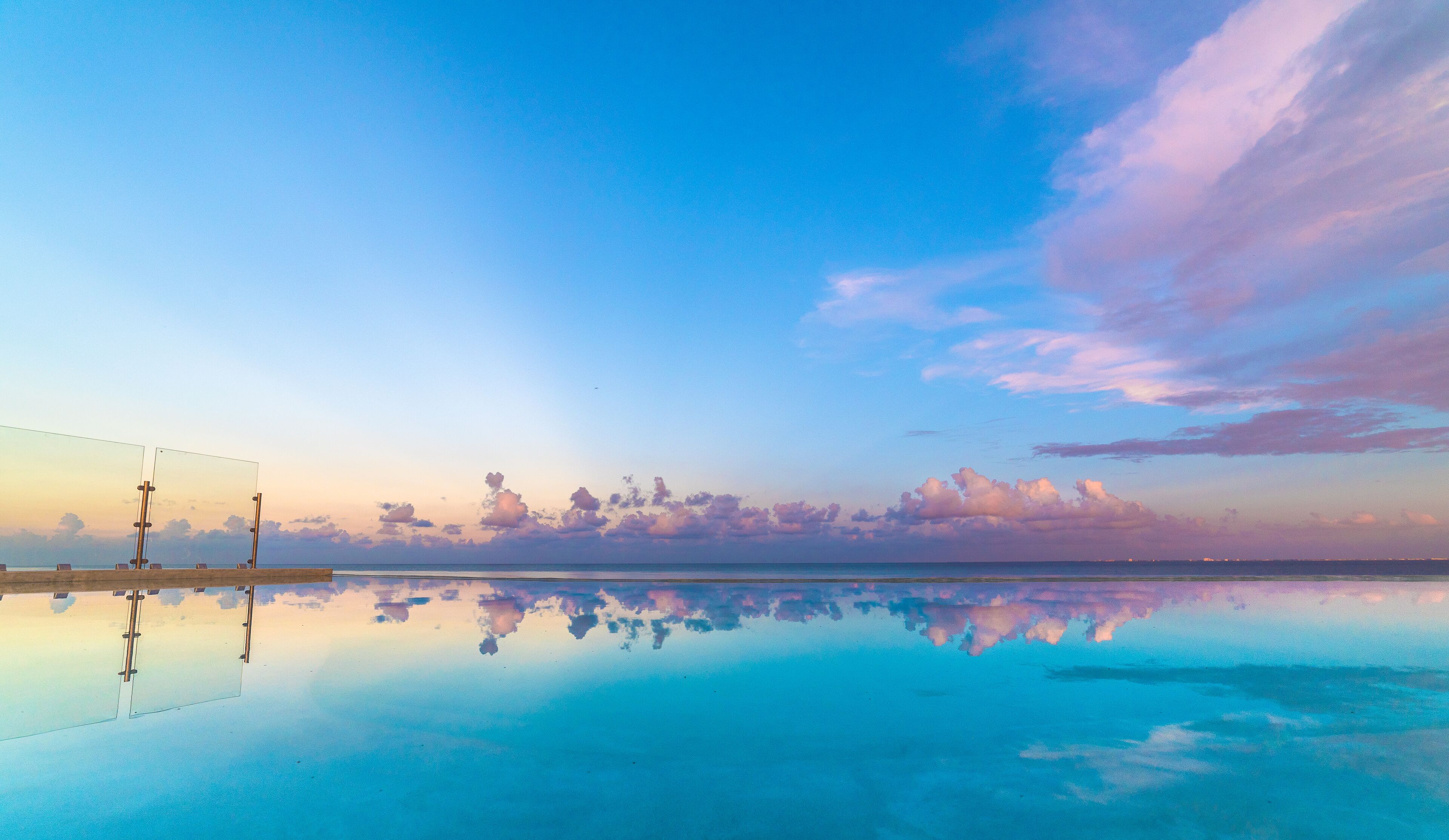 Uma praia tranquila, com águas calmas refletindo o céu e as nuvens.