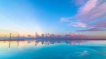 Uma praia tranquila, com águas calmas refletindo o céu e as nuvens.