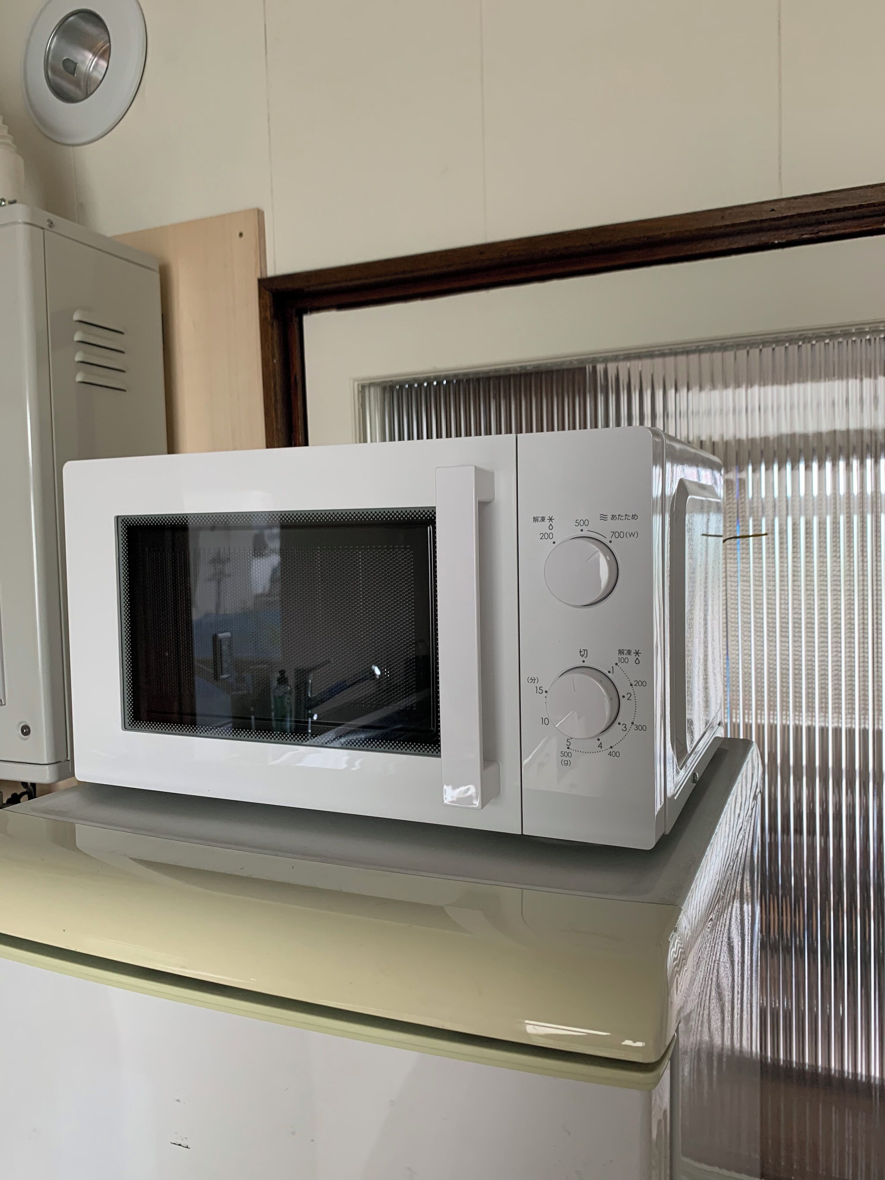 Um forno de micro-ondas branco com visor digital e painel de controle sobre uma mesa de vidro.