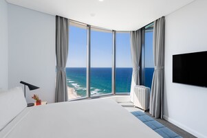 Quarto de hotel com uma cama grande, televisão de tela plana e vista para o oceano.