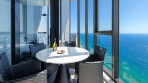 Quarto em um arranha-céu com vista panorâmica para o oceano, mobiliado com uma mesa redonda e cadeiras, e uma garrafa de champanhe.