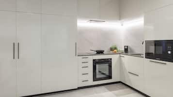 Uma cozinha moderna com armários em tons claros, forno embutido e micro-ondas.