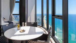 Quarto em um arranha-céu com vista panorâmica do oceano, uma mesa de jantar redonda com cadeiras e uma garrafa de champanhe.