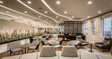 Um hall amplo com assentos modernos, balcão de recepção e uma parede decorativa.