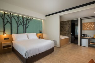 Quarto de hotel moderno com uma cama grande, um desenho de árvore na parede, uma pequena cozinha e um banheiro separado.