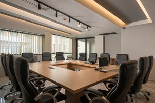 Uma sala de conferências com uma grande mesa retangular, cadeiras de couro preto e um design de teto moderno com iluminação em trilhos.