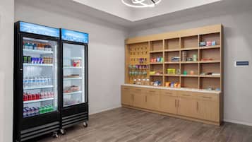 Uma cozinha compacta com geladeira repleta de bebidas, um armário de madeira com lanches e uma luminária no teto.