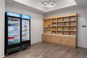 Uma cozinha compacta com geladeira repleta de bebidas, um armário de madeira com lanches e uma luminária no teto.