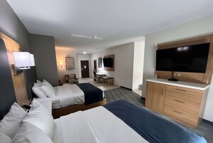 Quarto de hotel com duas camas, uma escrivaninha, uma cadeira, uma televisão e um guarda-roupa.