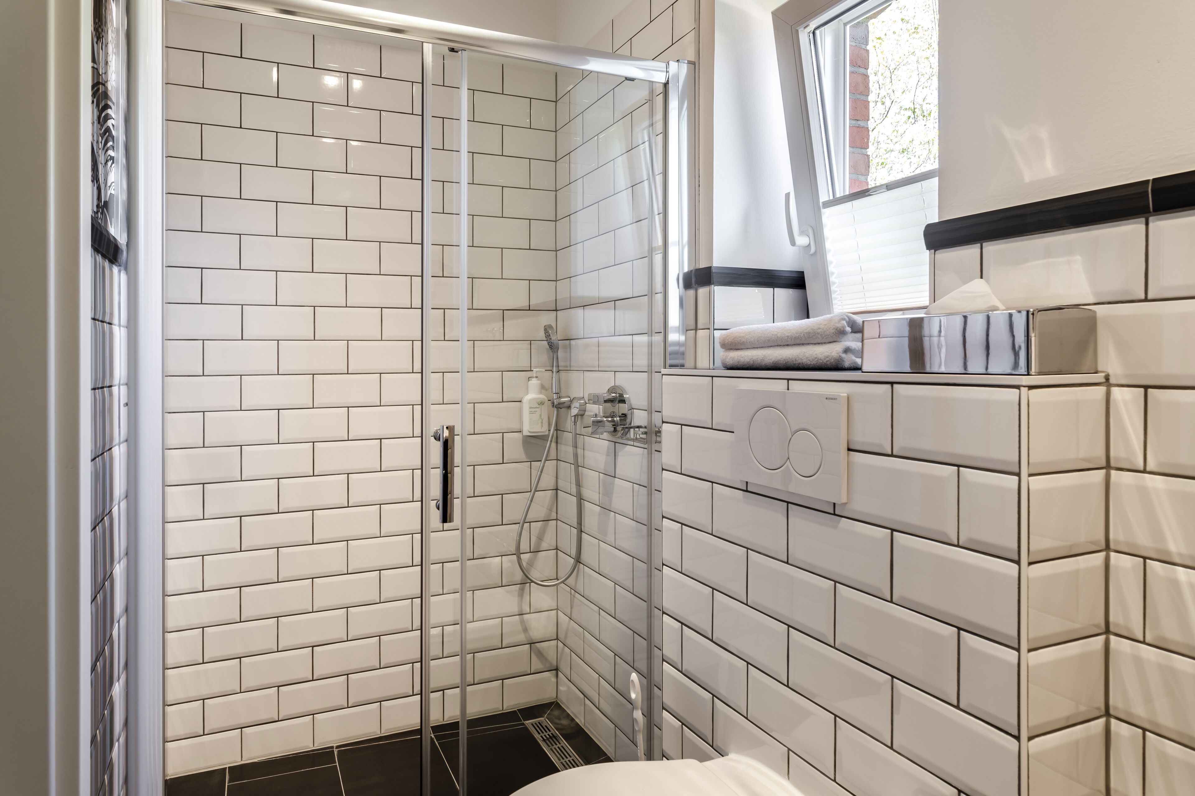 Casa de banho moderna com azulejos brancos tipo metrô, cabine de chuveiro em vidro e janela que oferece luz natural.