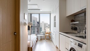 Cozinha compacta e moderna, equipada com máquina de lavar e secar integradas, pequena área de refeições e uma janela ampla com vista para a cidade.