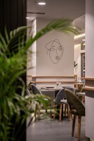 Uma sala de jantar moderna com design minimalista, apresentando uma parede branca com um desenho linear simples, cadeiras de madeira e uma mesa posta para dois.