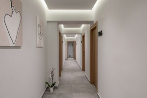Um corredor moderno com design minimalista, apresentando um caminho reto, portas de madeira e um vaso de planta.