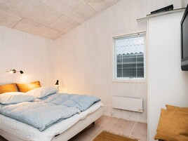 Quarto com cama, janela com persianas, TV fixada na parede e radiador.