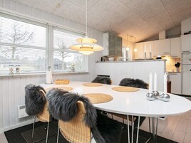 Uma sala de jantar moderna com uma mesa redonda, cadeiras com detalhes em pele e um lustre pendente.