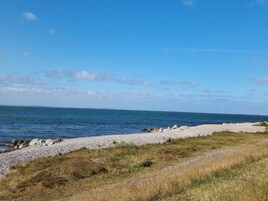 Paisagem costeira com praia de pedras, áreas gramadas e céu azul límpido.