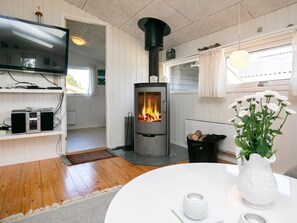 Quarto acolhedor com lareira a lenha, televisão em uma prateleira e uma mesa branca com um vaso e uma vela.