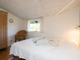 Quarto com cama, cadeira, janela e guarda-roupa de madeira.
