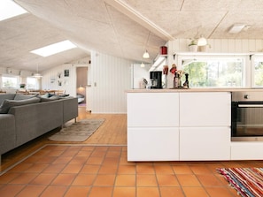Cozinha moderna com armários brancos, forno embutido e área de jantar com sofá cinza e mesa de madeira.
