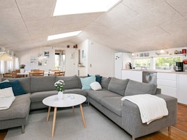 Uma sala de estar moderna com um sofá seccional cinza, uma mesa de centro redonda e uma área de jantar com cadeiras de madeira.