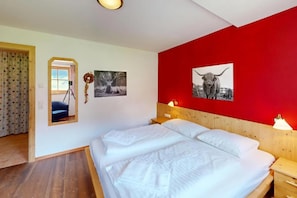 Quarto com uma cama, um espelho, um quadro de um touro e uma parede vermelha.