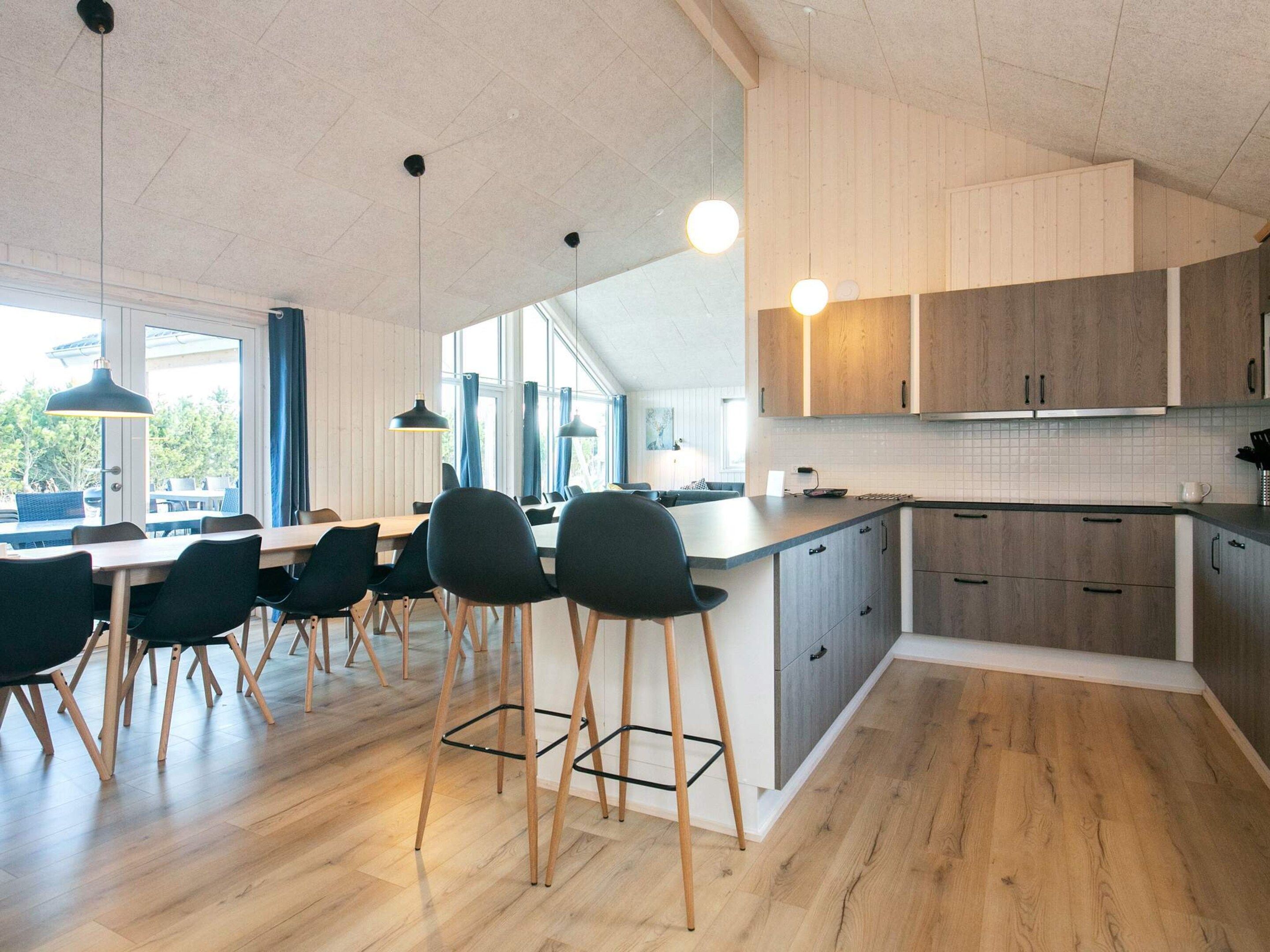 Cozinha moderna com armários de madeira, área de refeições com cadeiras e uma grande janela que traz luz natural.