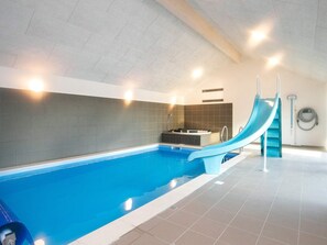 Piscina interna com um escorregador azul, uma banheira de hidromassagem e um esfregão na parede.